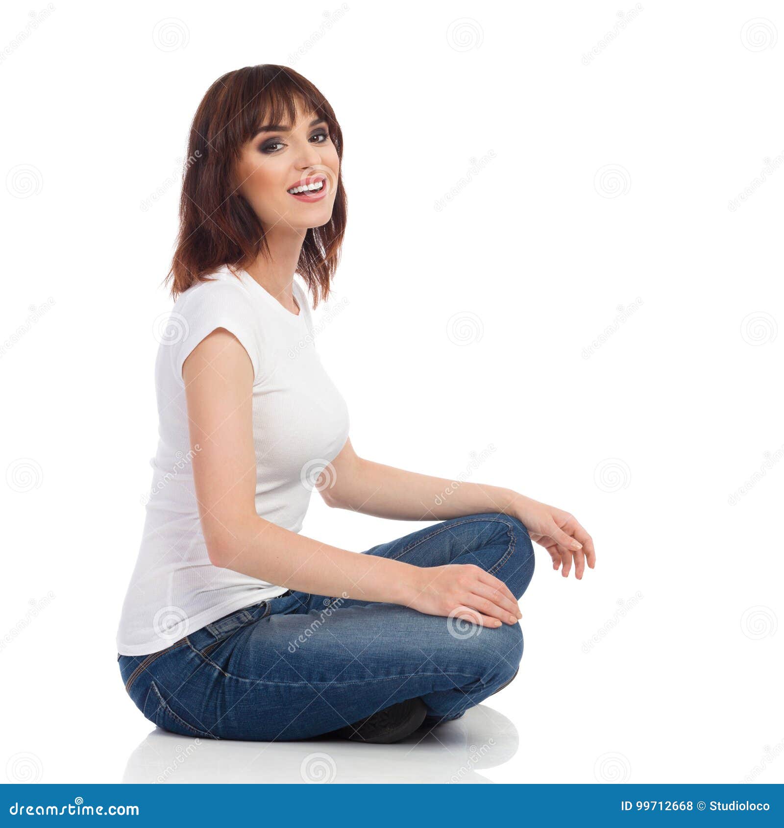 Smiling Young Woman Is Sitting On A Floor With Crossed Legs And Looking