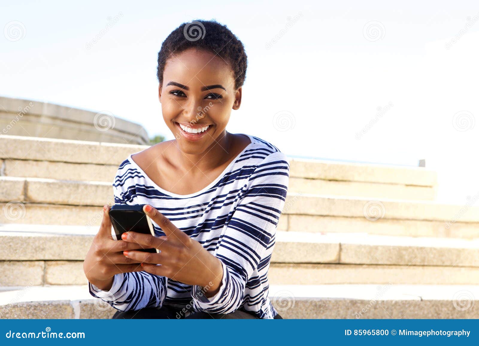 Smiling Young Woman Sitting Outside Using Cellphone Stock Photo - Image ...