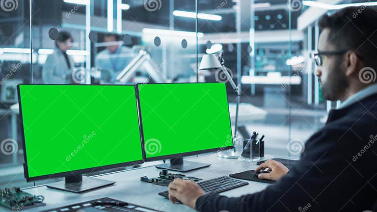 Software Developer Working On A Desktop Computer With Two Green Screen Chromakey Display Screens
