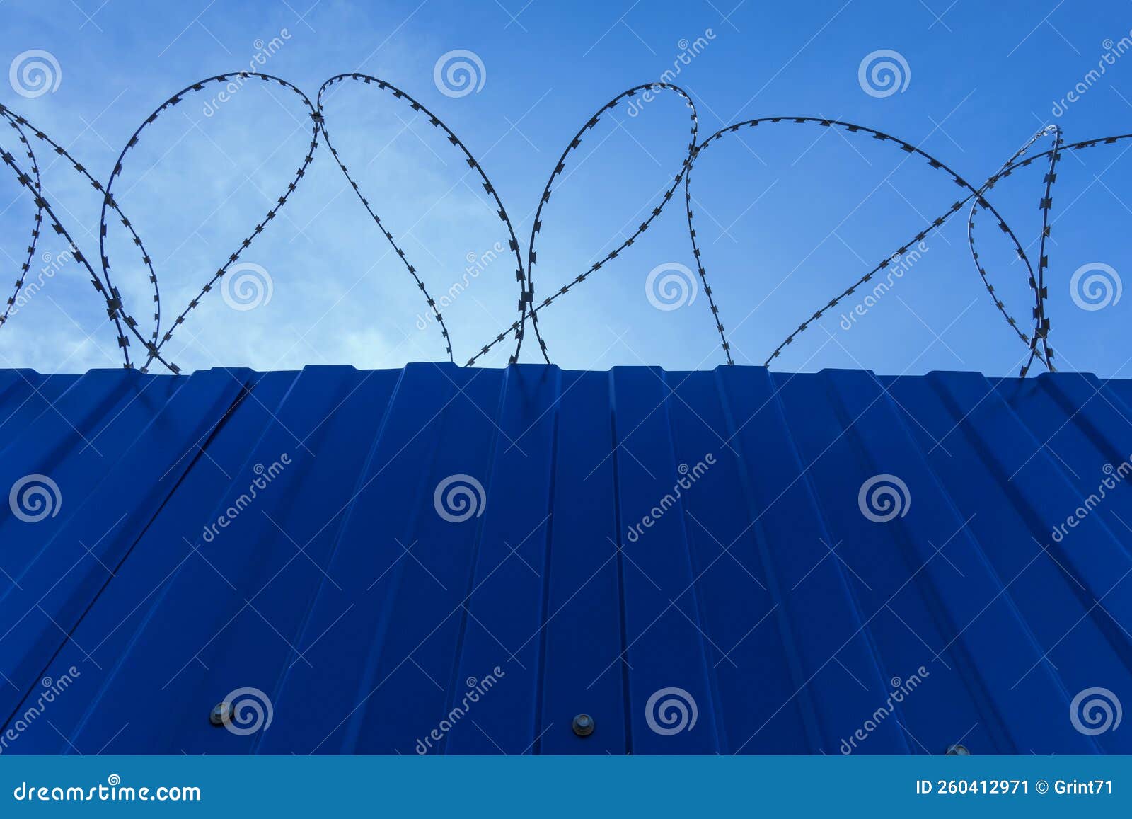 Solid, Blue Iron Fence with Barbed Wire Under a Blue Sky Stock Image ...