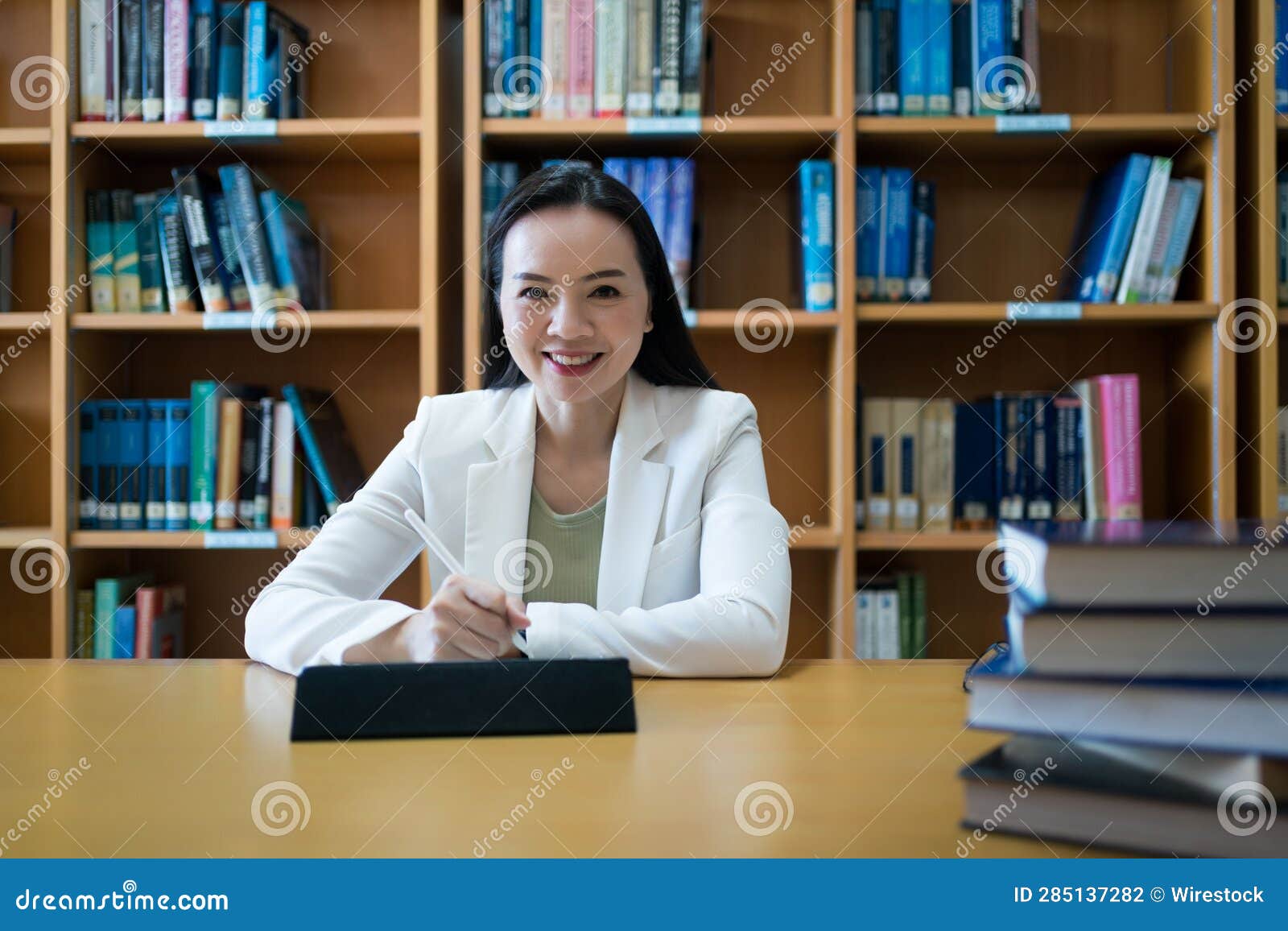 Southeast Asian Female Lecturer Sits at a Small Table, Working at the ...