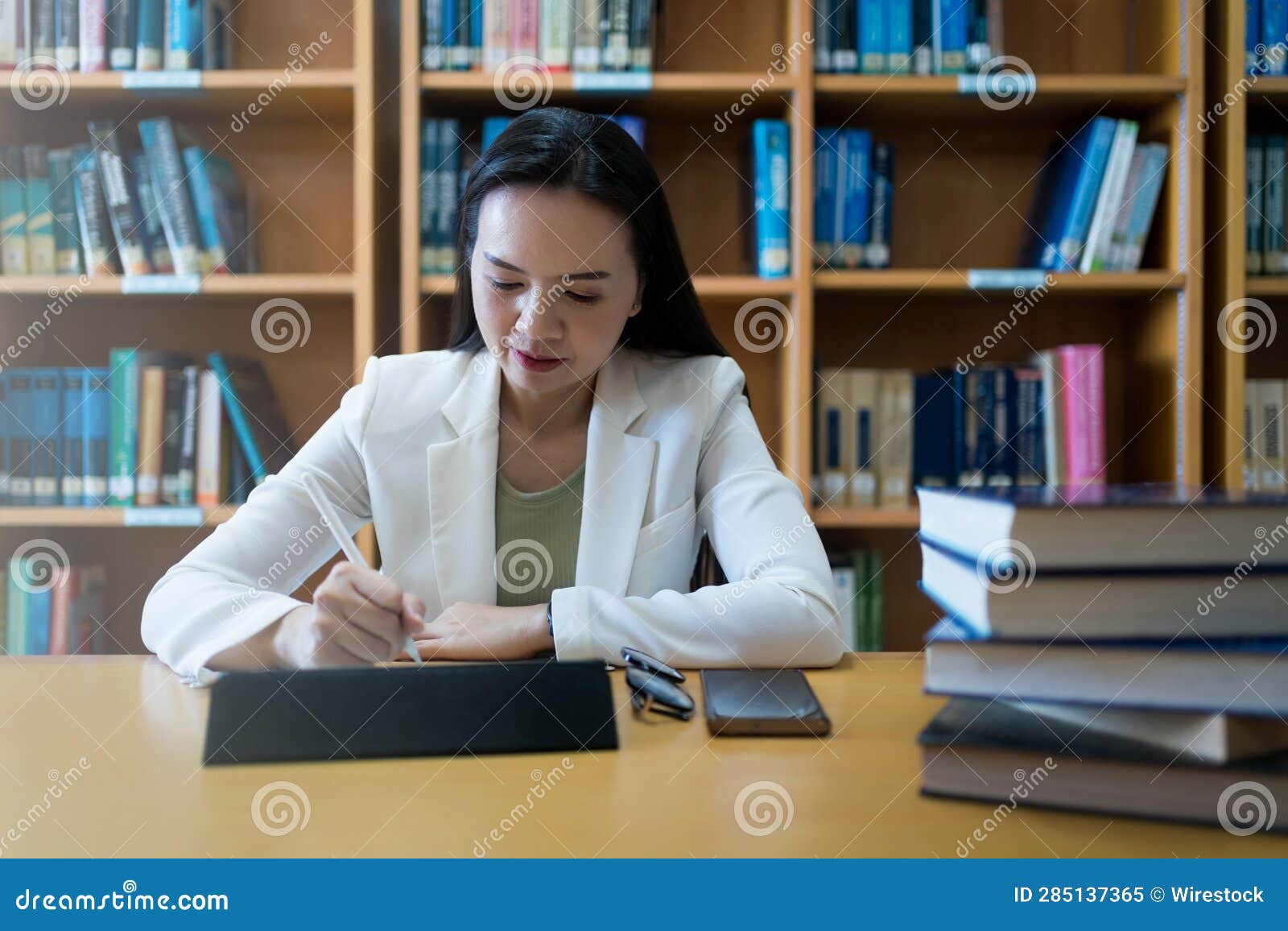 Southeast Asian Female Lecturer Sits at a Small Table, Working at the ...