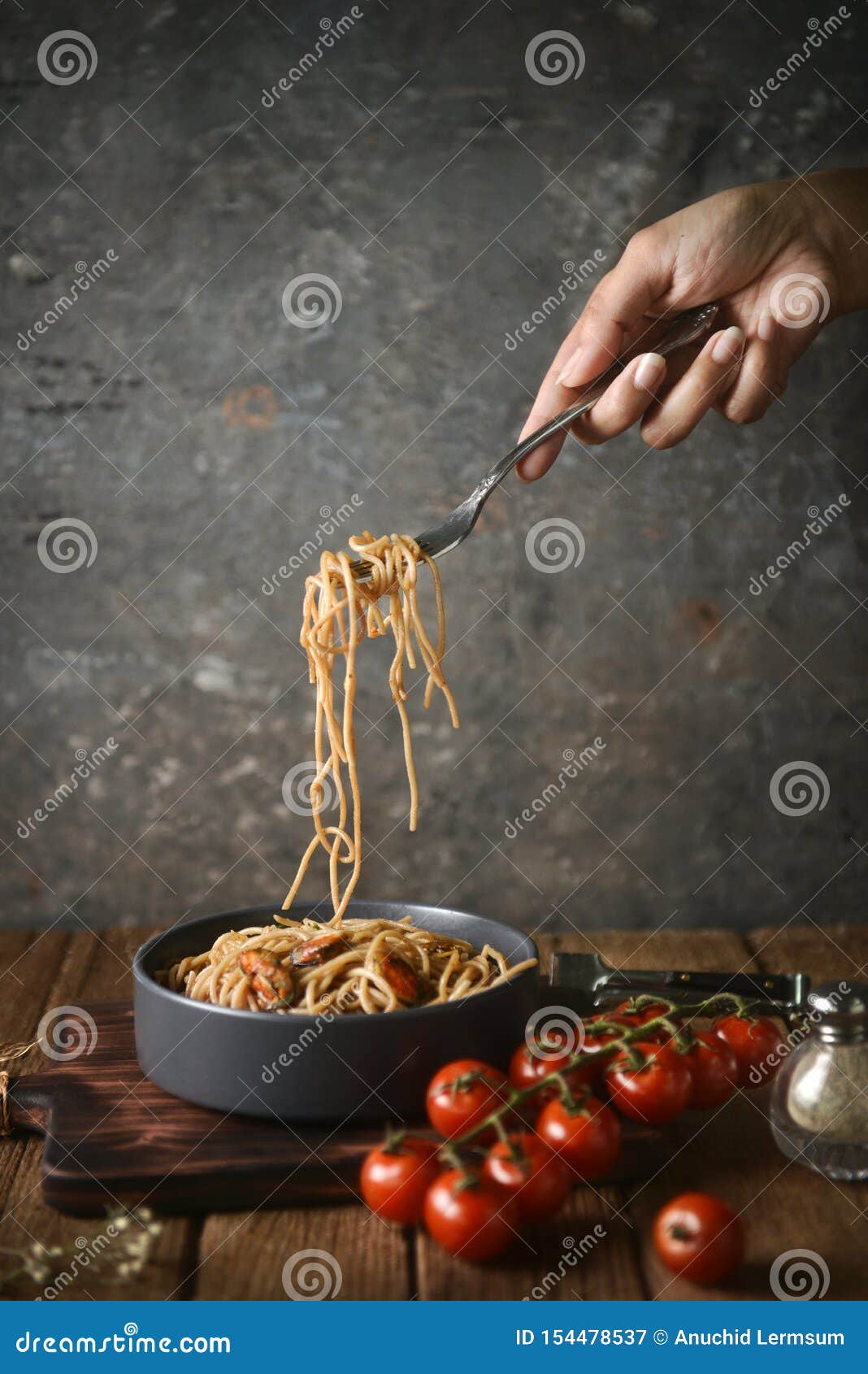 Spaghetti is Pulled Up by the Fork in Hand from Dish and Wooden Plate ...