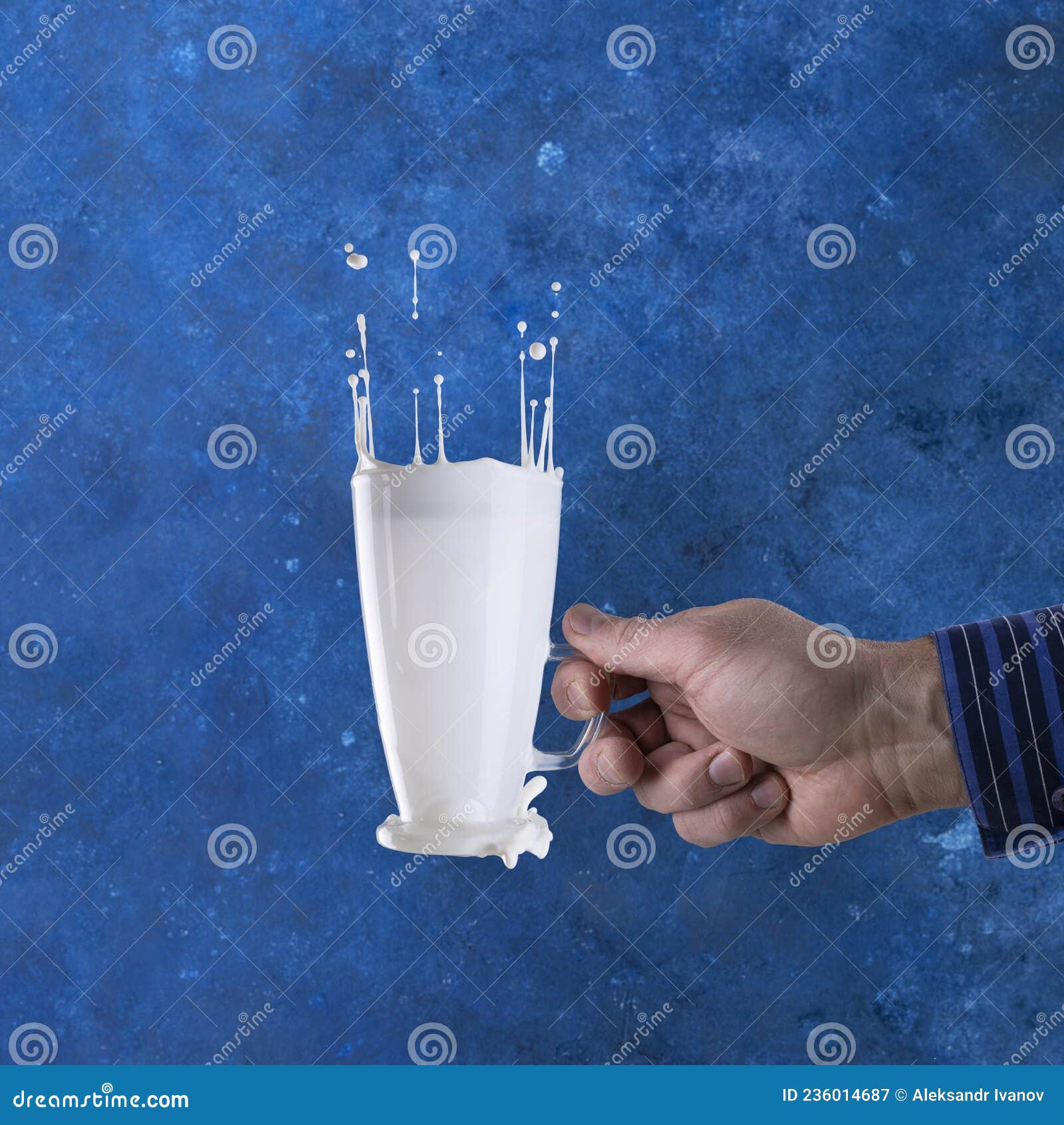 Splashes of Milk in a Glass Levitation on a Blue Background with a Hand ...