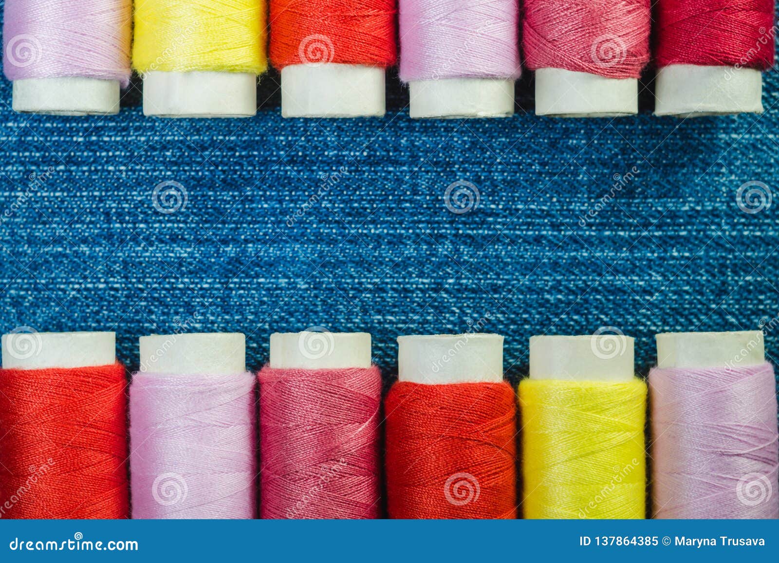 Spools of Colored Sewing Thread Arranged in Two Rows on Blue Denim with ...