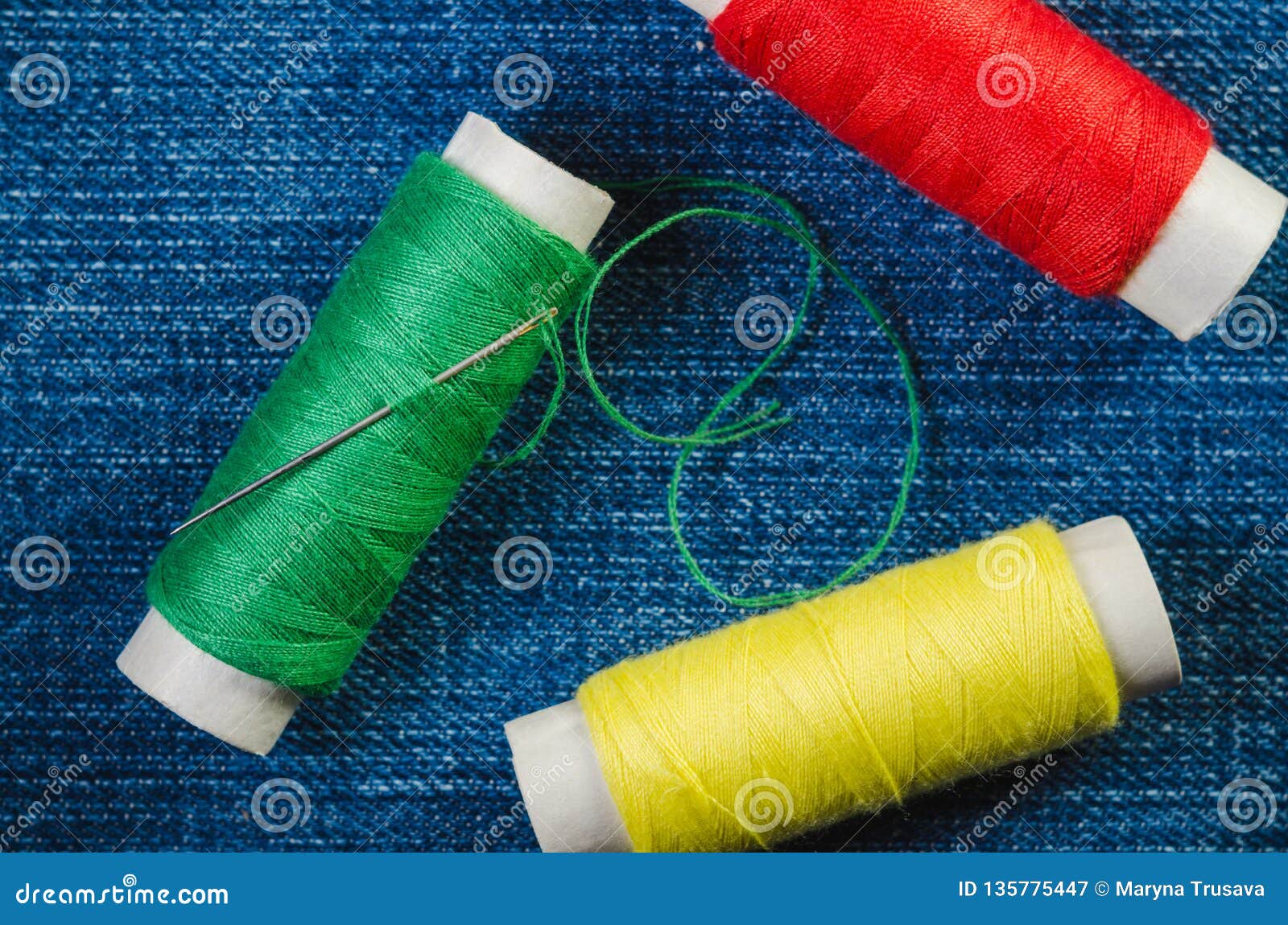 Spools of Green, Red and Yellow Threads and Sewing Needle on Denim ...
