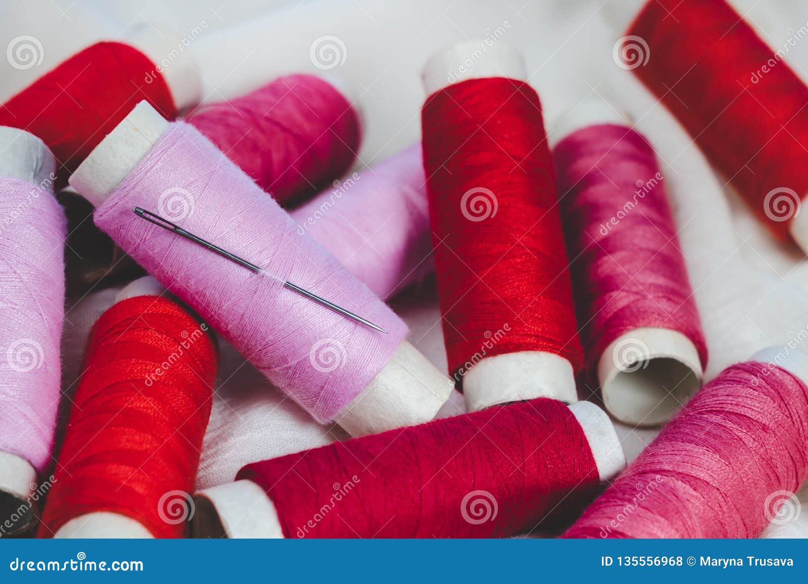 Spools of Pink and Red Threads and Sewing Needle on White Cotton Cloth ...