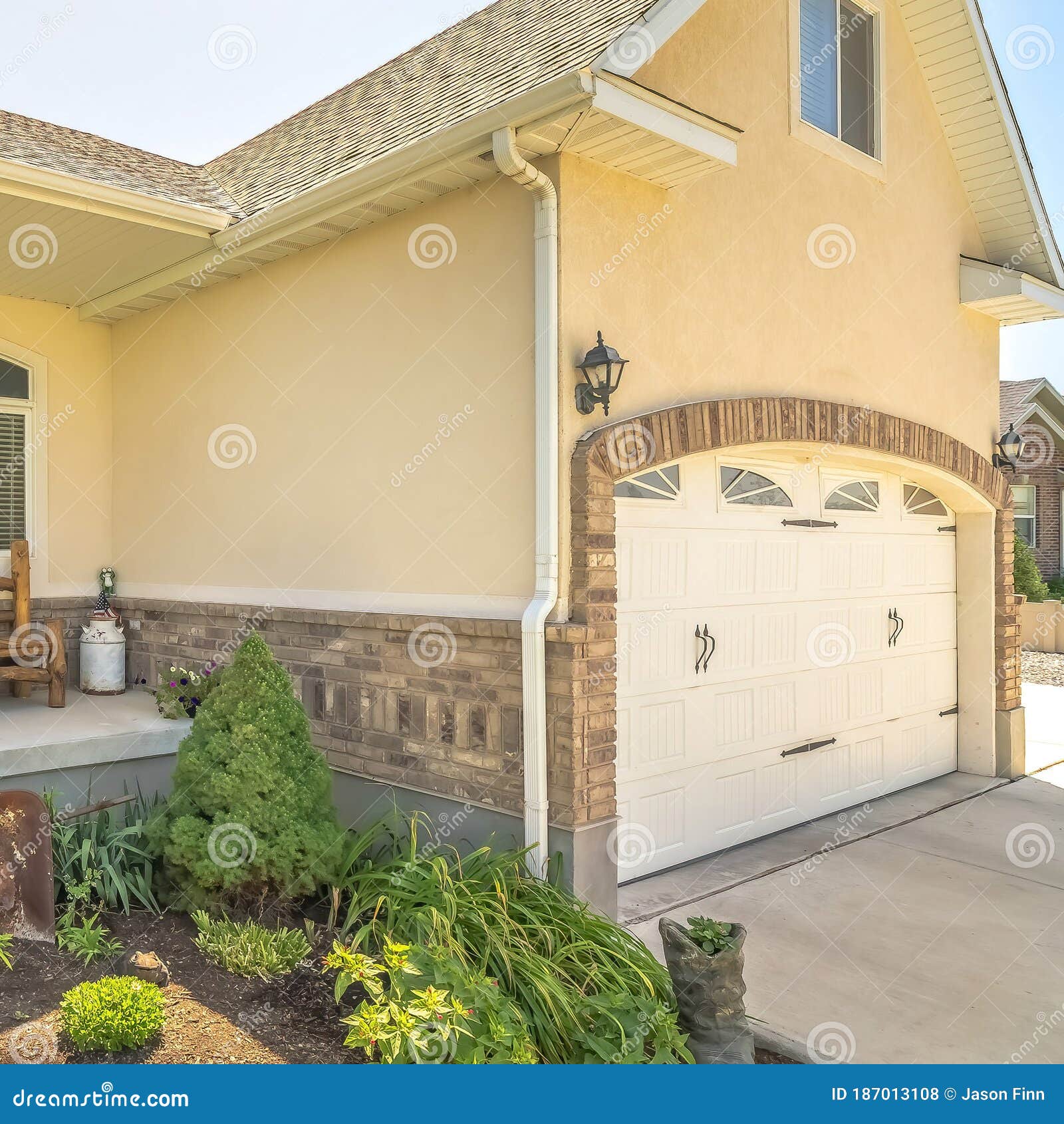 Square Home Facade With View Of Arched Garage Door And Front Door With Oval Glass Pane Stock