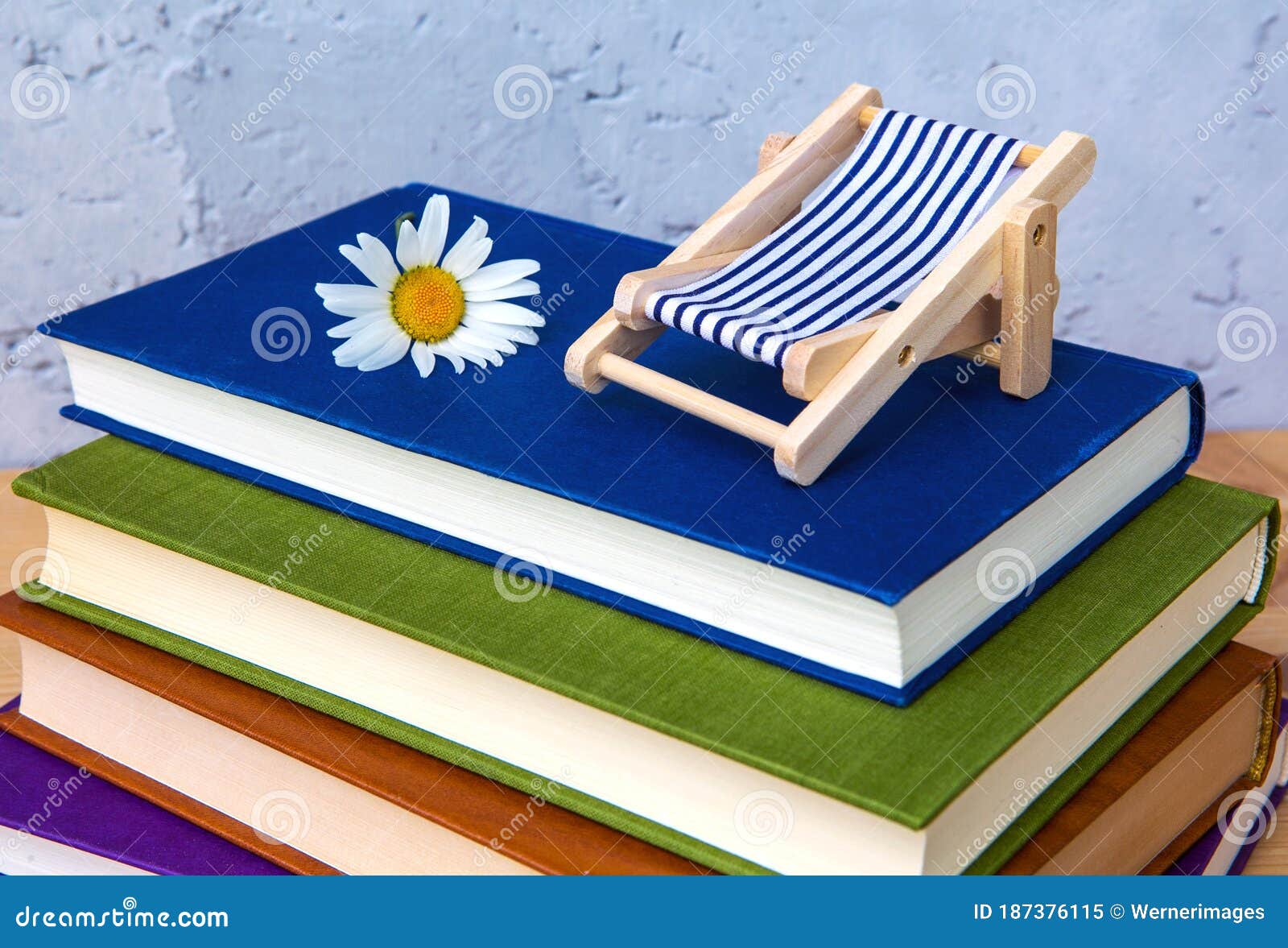 Stack of Books and a Miniature Lounger and a Daisy on Wooden Table ...