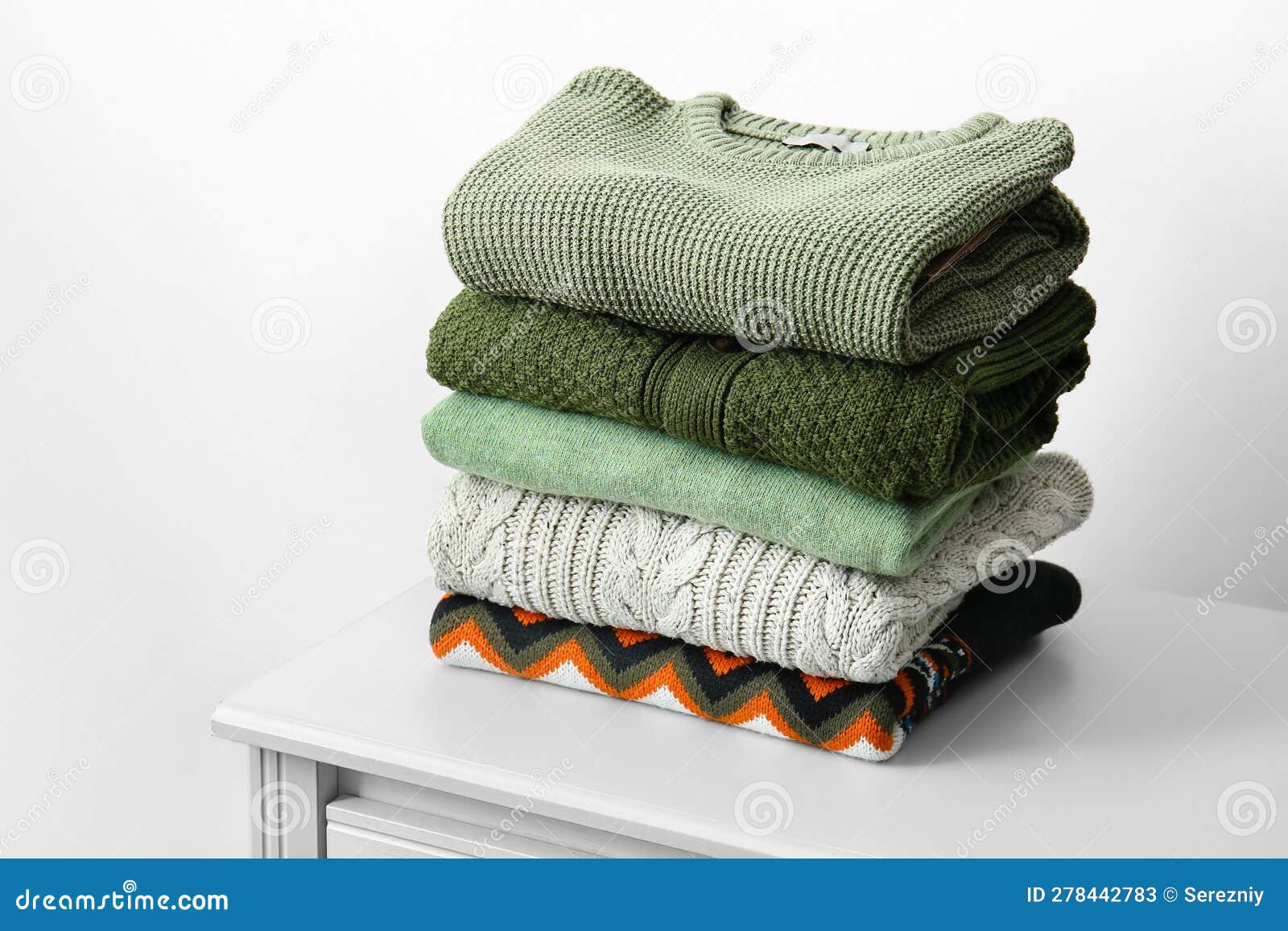 Stack of Different Stylish Sweaters on Table Near Light Wall Stock ...