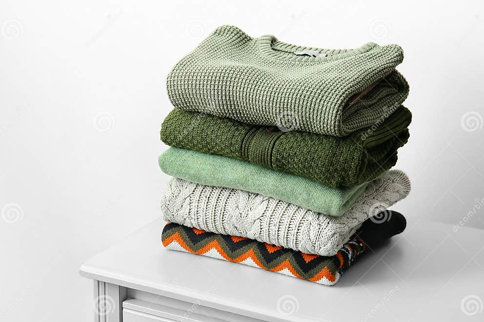 Stack of Different Stylish Sweaters on Table Near Light Wall Stock ...