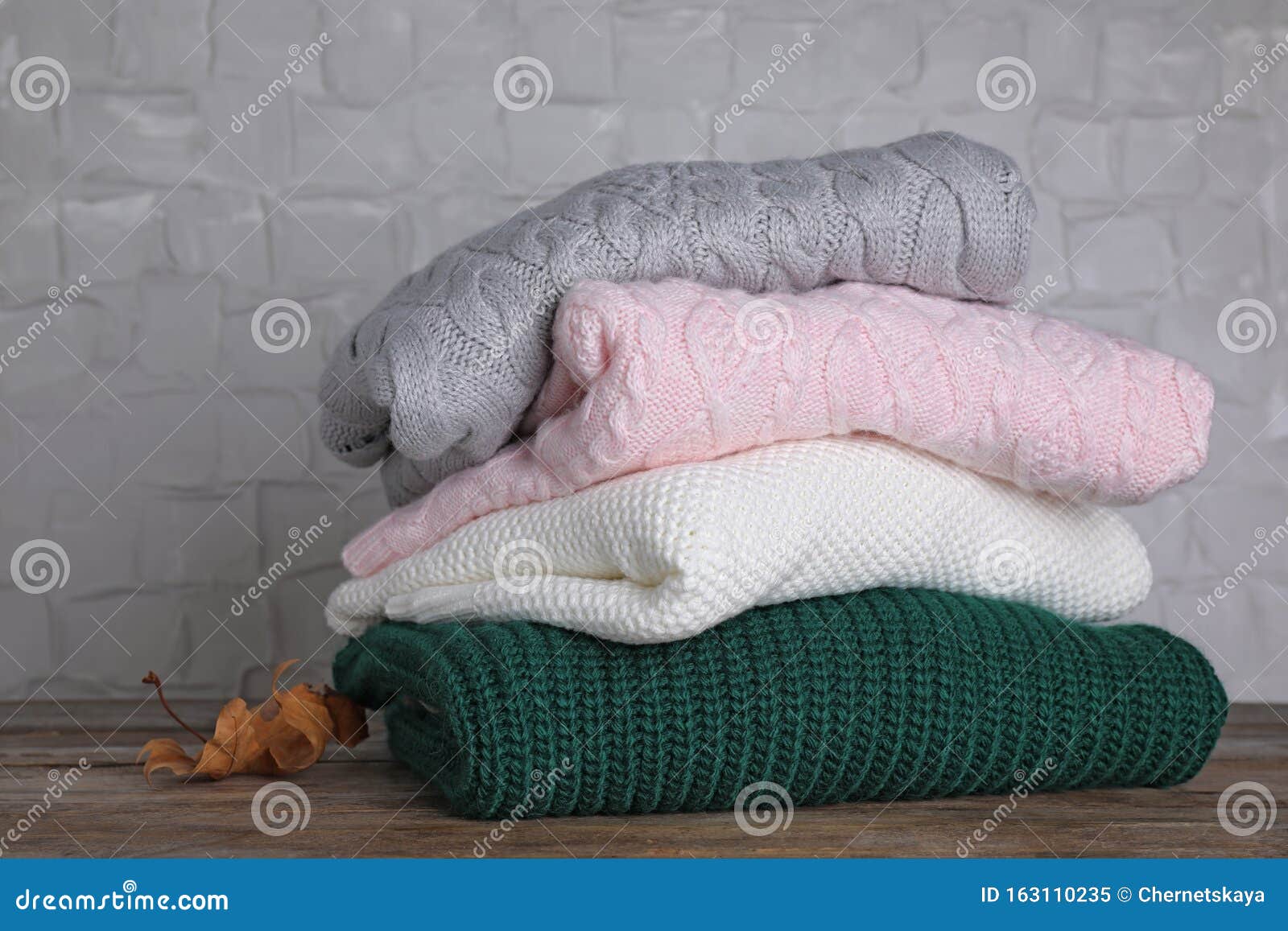 Stack of Folded Knitted Sweaters and Autumn Leaf on Table Against White ...
