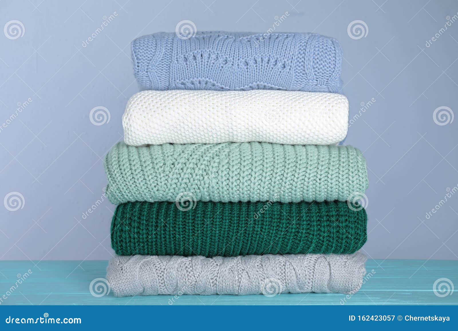 Stack of Folded Knitted Sweaters on Blue Table Against Grey Background ...