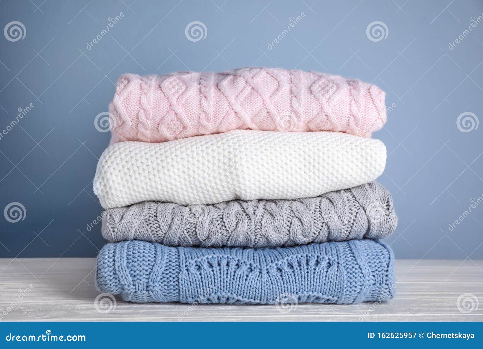 Stack of Folded Knitted Sweaters on White Table Against Grey Background ...