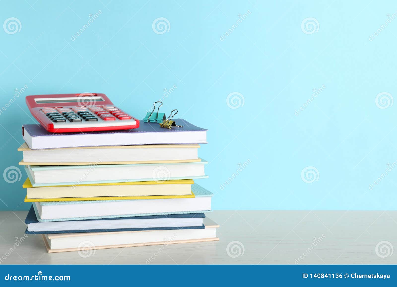 Stack of Hardcover Books and Calculator on Table Against Color ...