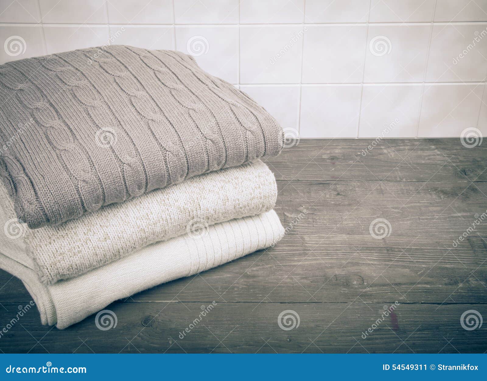 Stack of Knitted Clothes on Wooden Table Opposite a Light Tile Wall ...