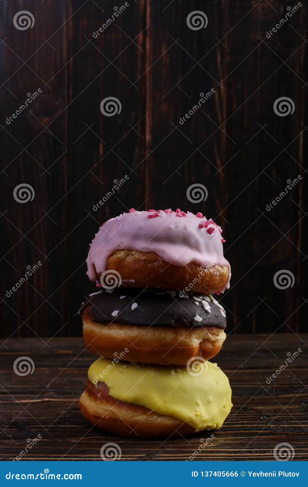 A Stack of Multi-colored Donuts with Icing and Powder on a Wooden Table ...