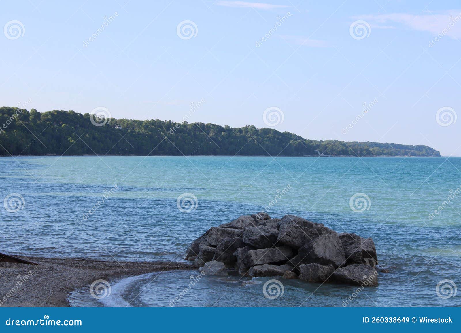 Stack of Rocks on the Lakeshore with Clear Blue Water and Green Forests ...
