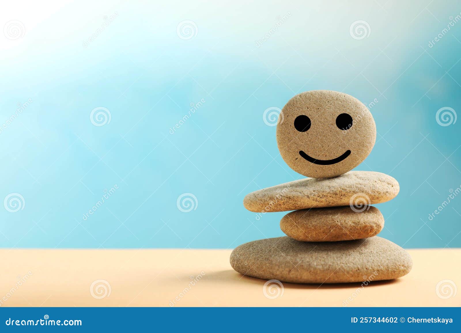 Stack of Stones with Drawn Happy Face on Beige Table Against Light Blue ...