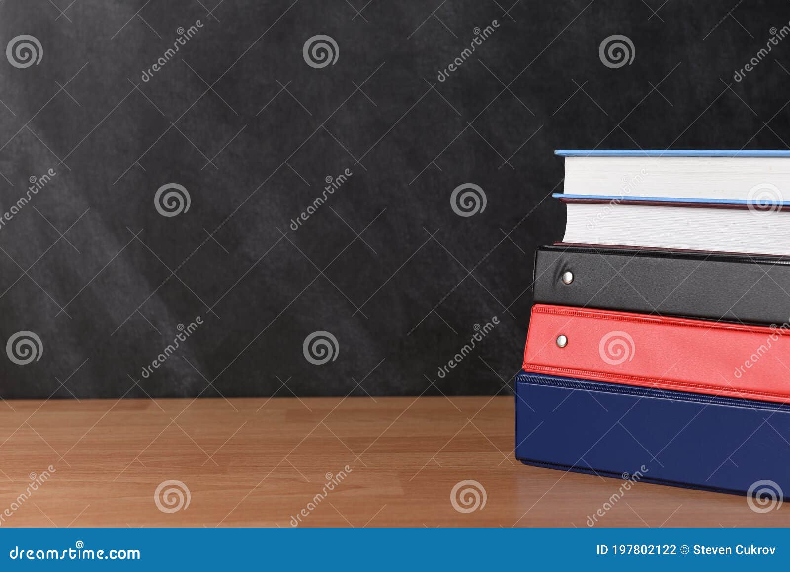 A Stack of Three Different Binders on Desk in Front of Black Board with ...