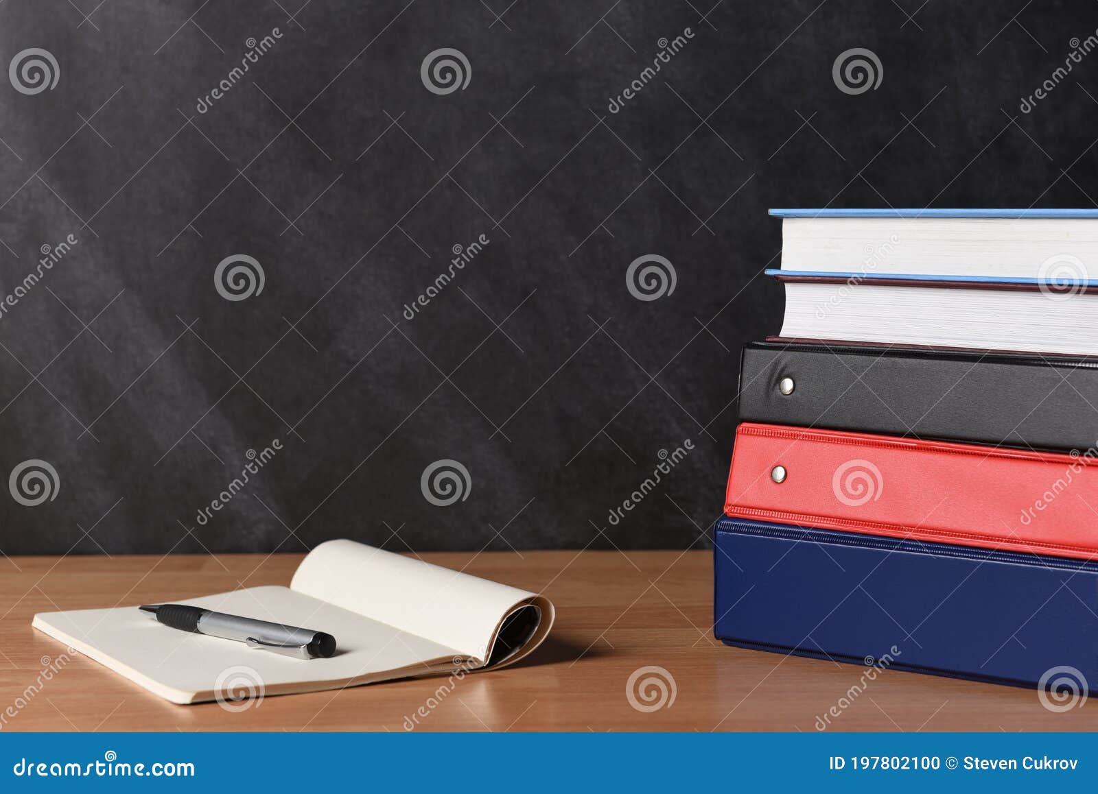 A Stack of Three Different Binders on Desk in Front of Black Board with ...