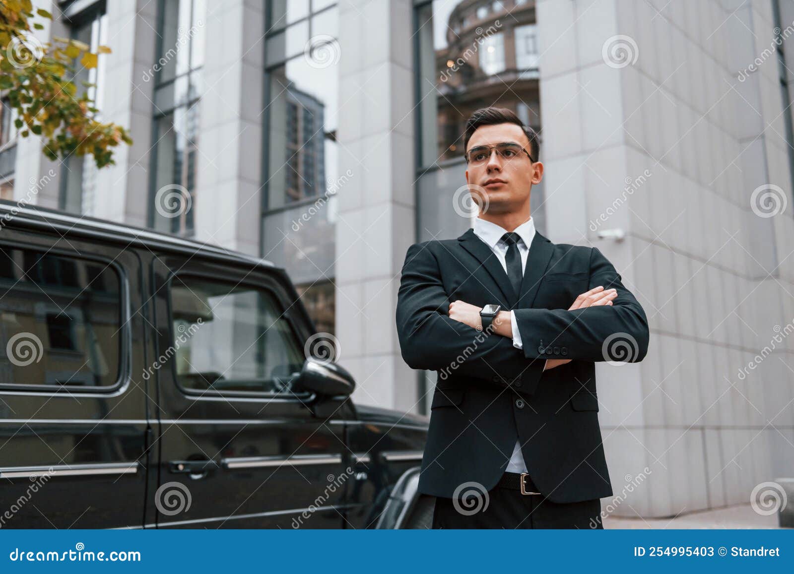 Standing With Arms Crossed Businessman In Black Suit And Tie Is