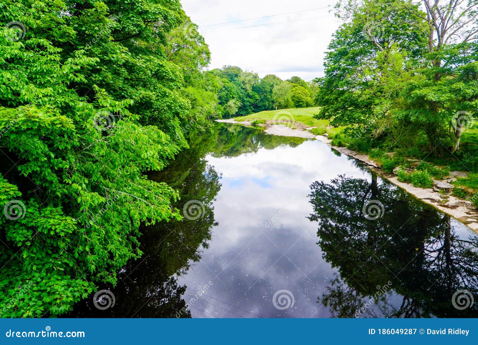 Standing on a Bridge Looking Down a Slow Moving River with Green Banks ...