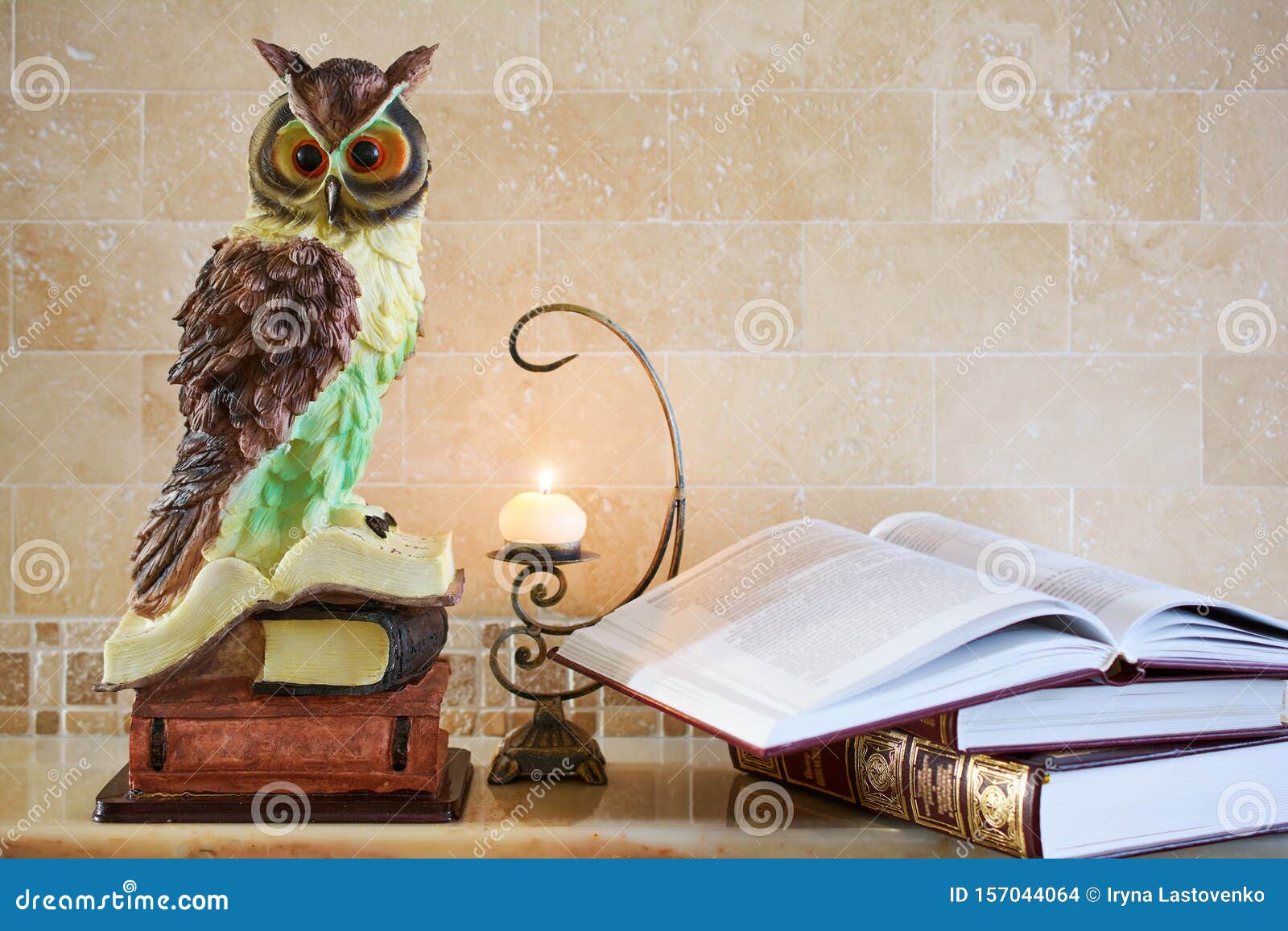 Statuette of an Owl, a Stack of Books with an Open Book and a Lit ...