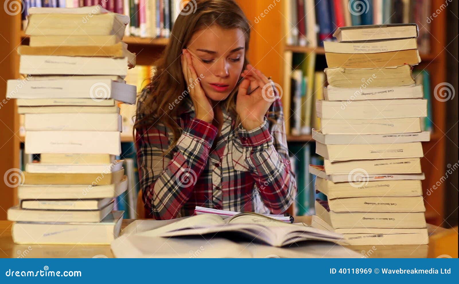 Stressed Student Studying and Taking Notes in the Library Surrounded by ...