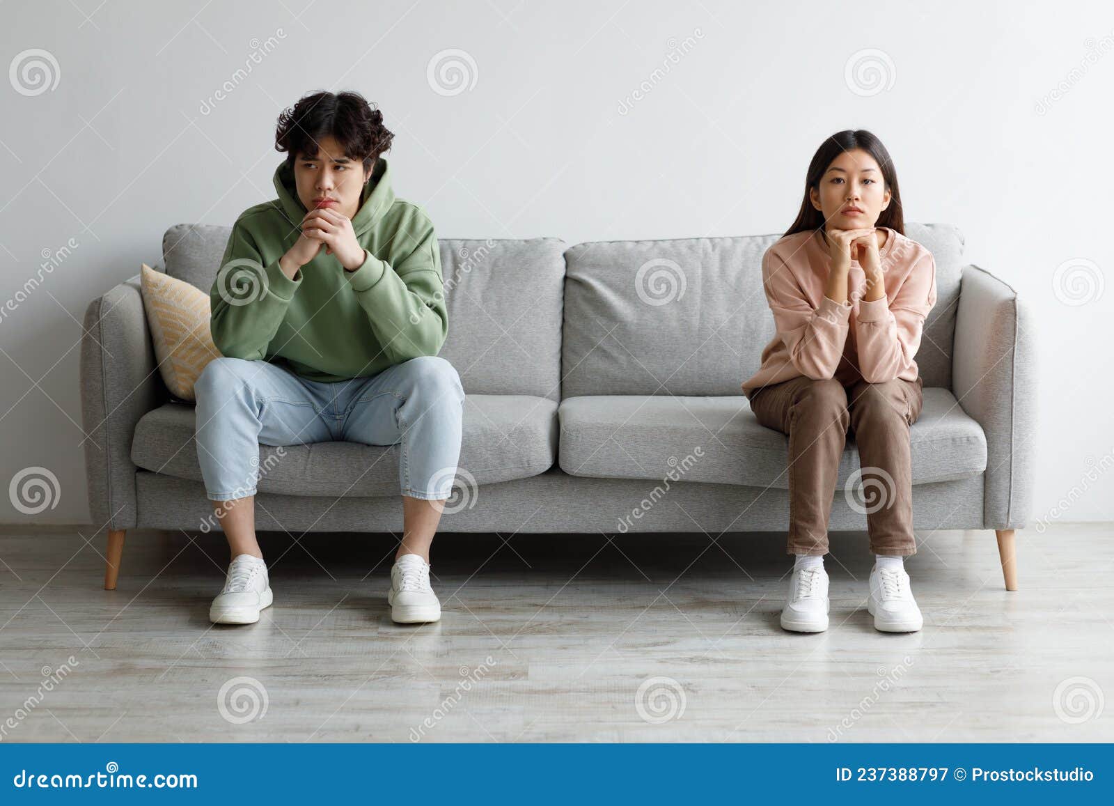 Stubborn Young Asian Couple Sitting On Opposite Sides Of Couch In