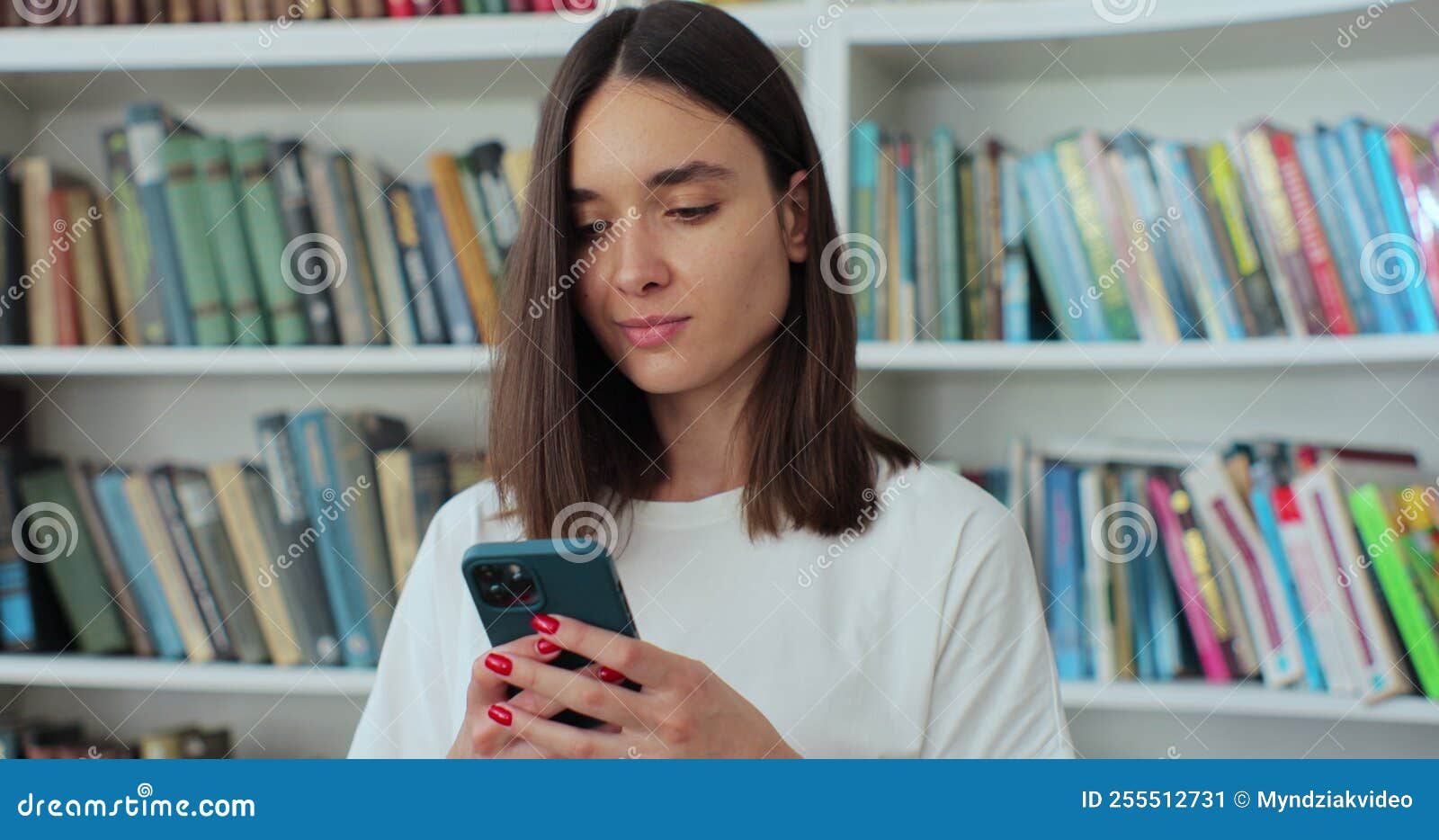 Student Girl Standing in Library and Using Smartphone, Texting Message ...