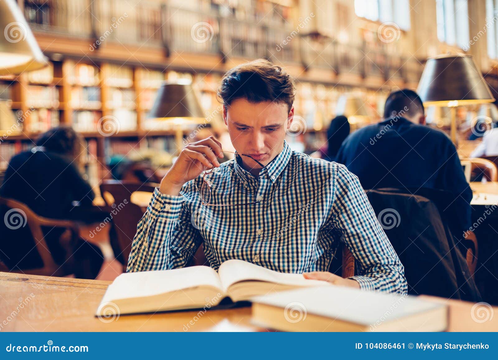 Student Man Sitting On The Desk In Library Reading Room And Doing ...