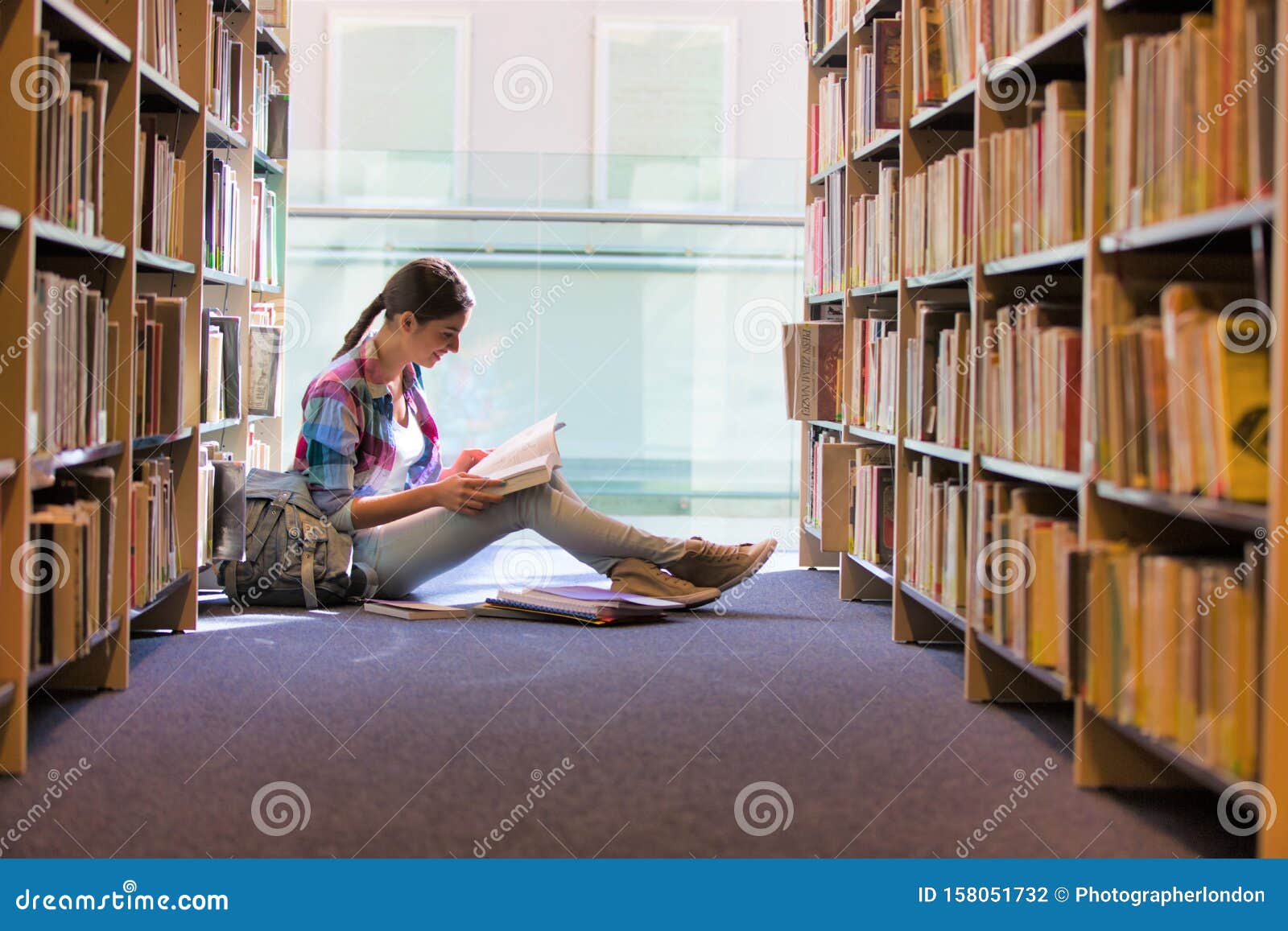 Student Reading Book while Sitting Against Bookshelf at Library Stock ...