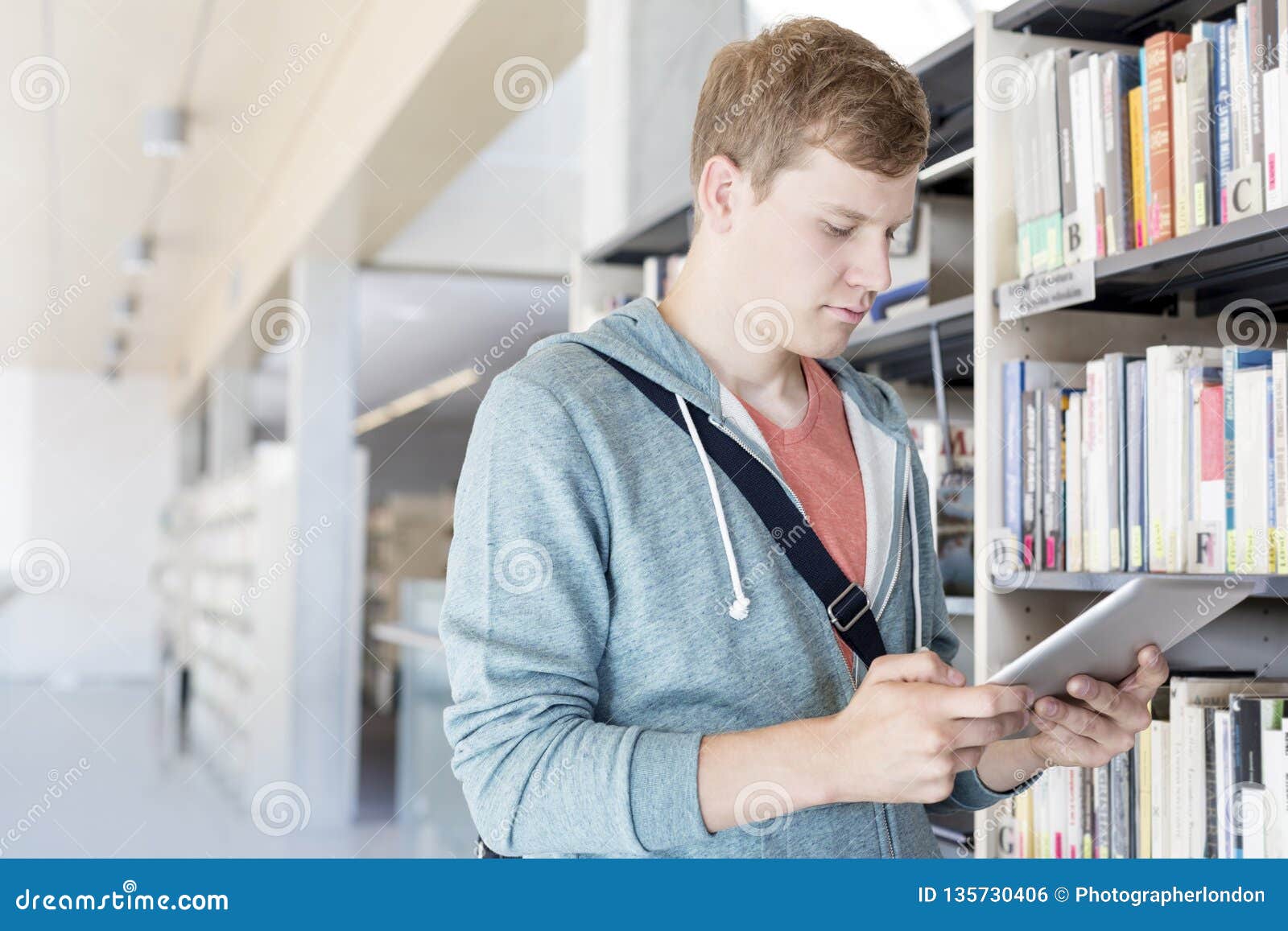 Student Using Digital Tablet while Standing by Bookshelf at Library ... Student Using Digital Tablet while Standing by Bookshelf at Library ...