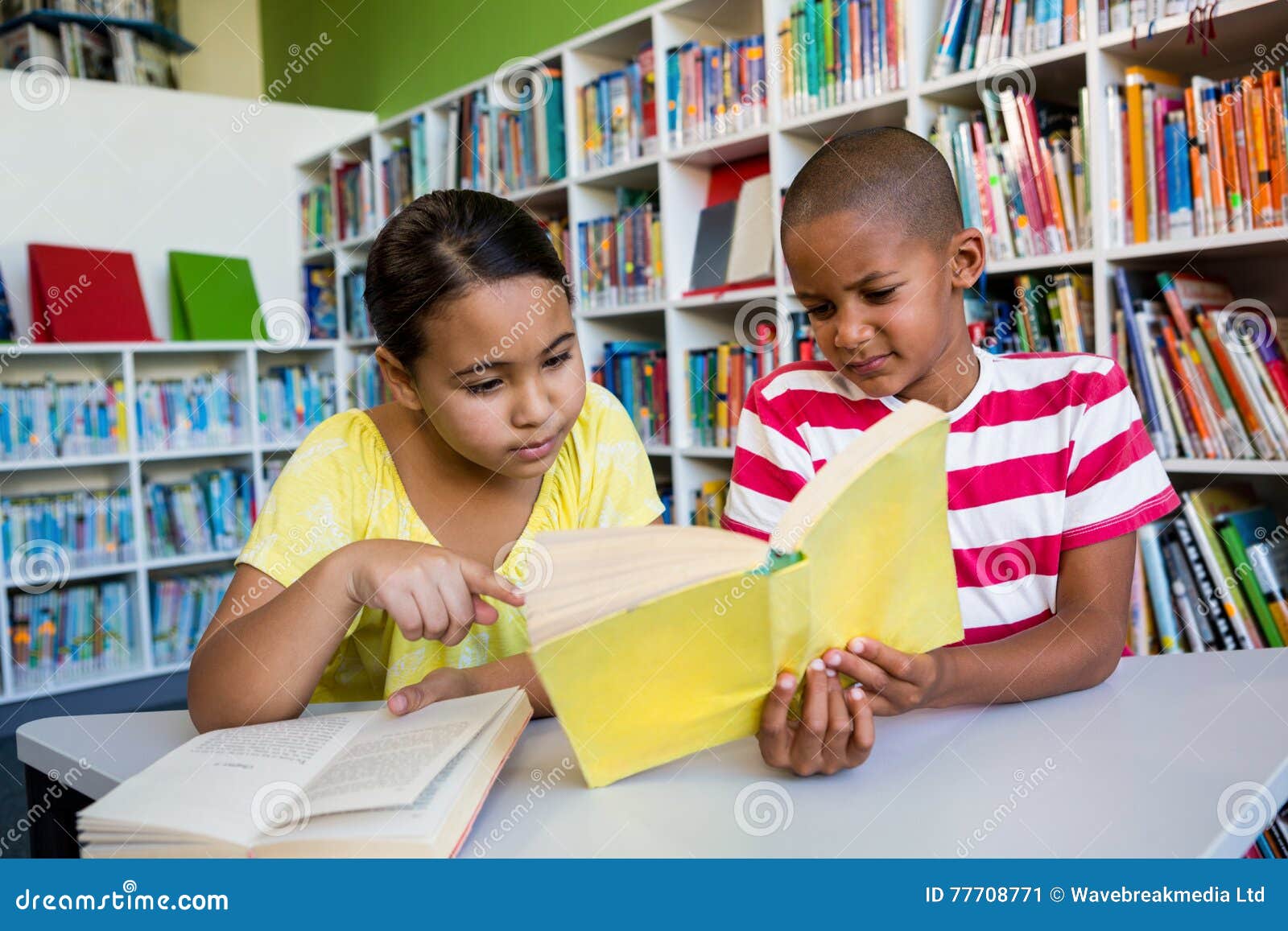 Students Reading Book Against Bookshelf at Library in School Stock ...