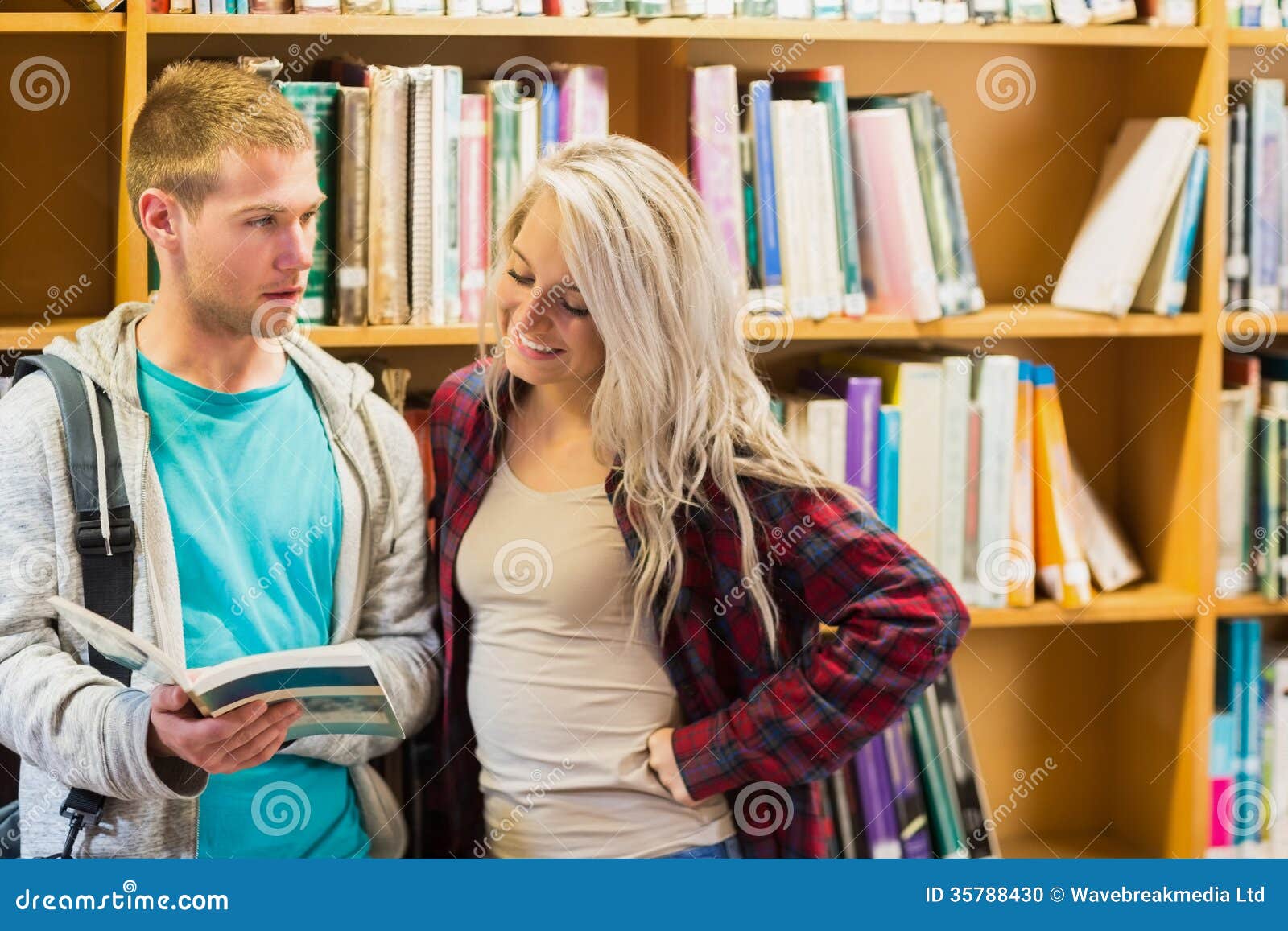 Students Reading Book Against Bookshelves in Library Stock Photo ...
