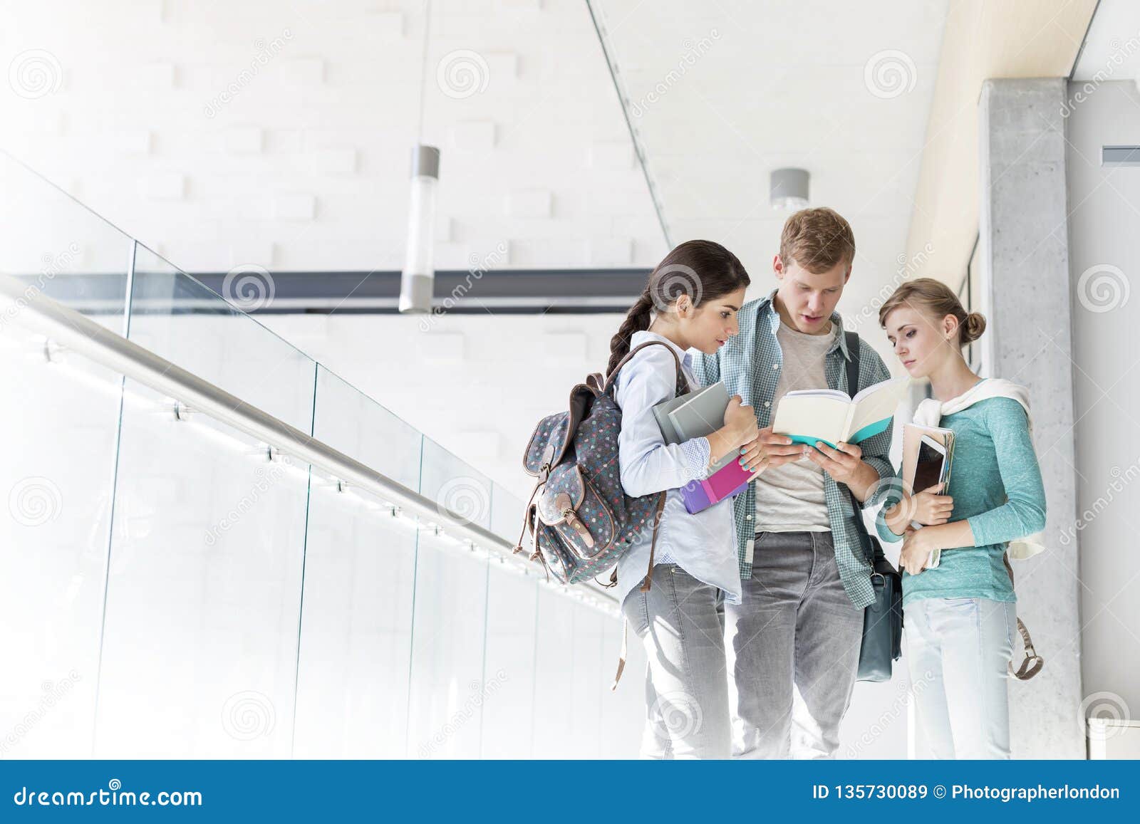 Friends Discussing Over Book while Standing in Corridor at University ...