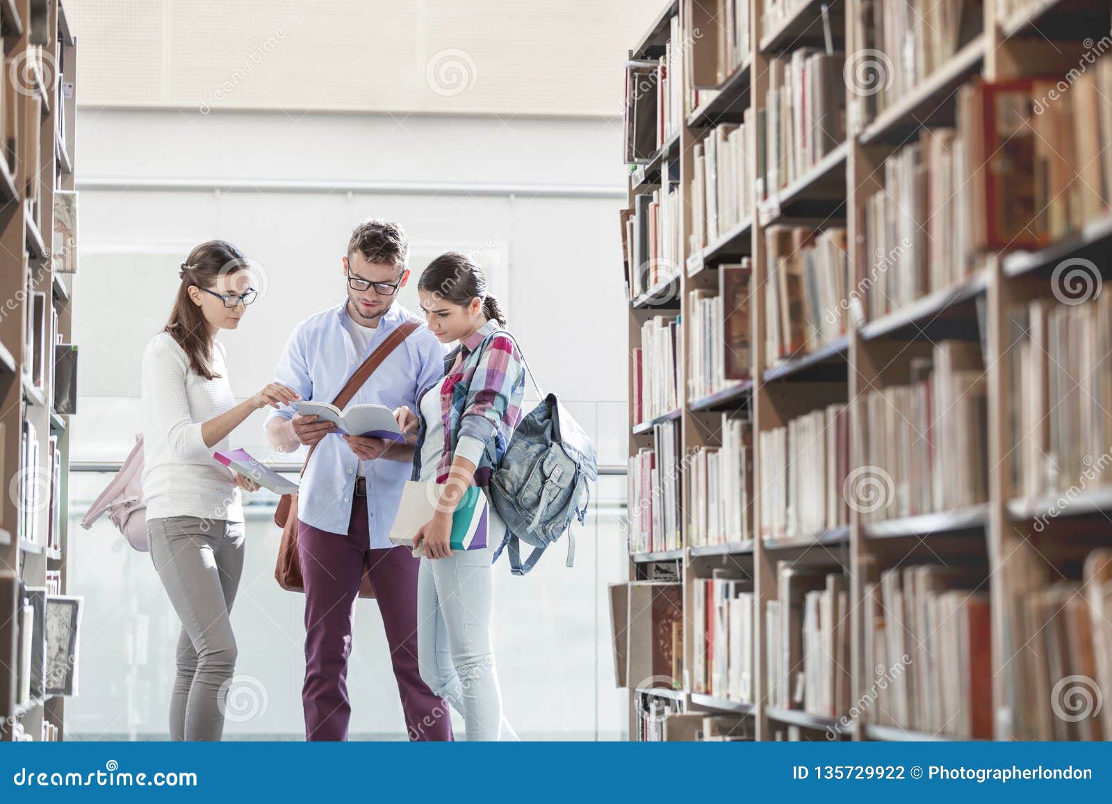 Friends Discussing while Reading Book at Library in University Stock ...