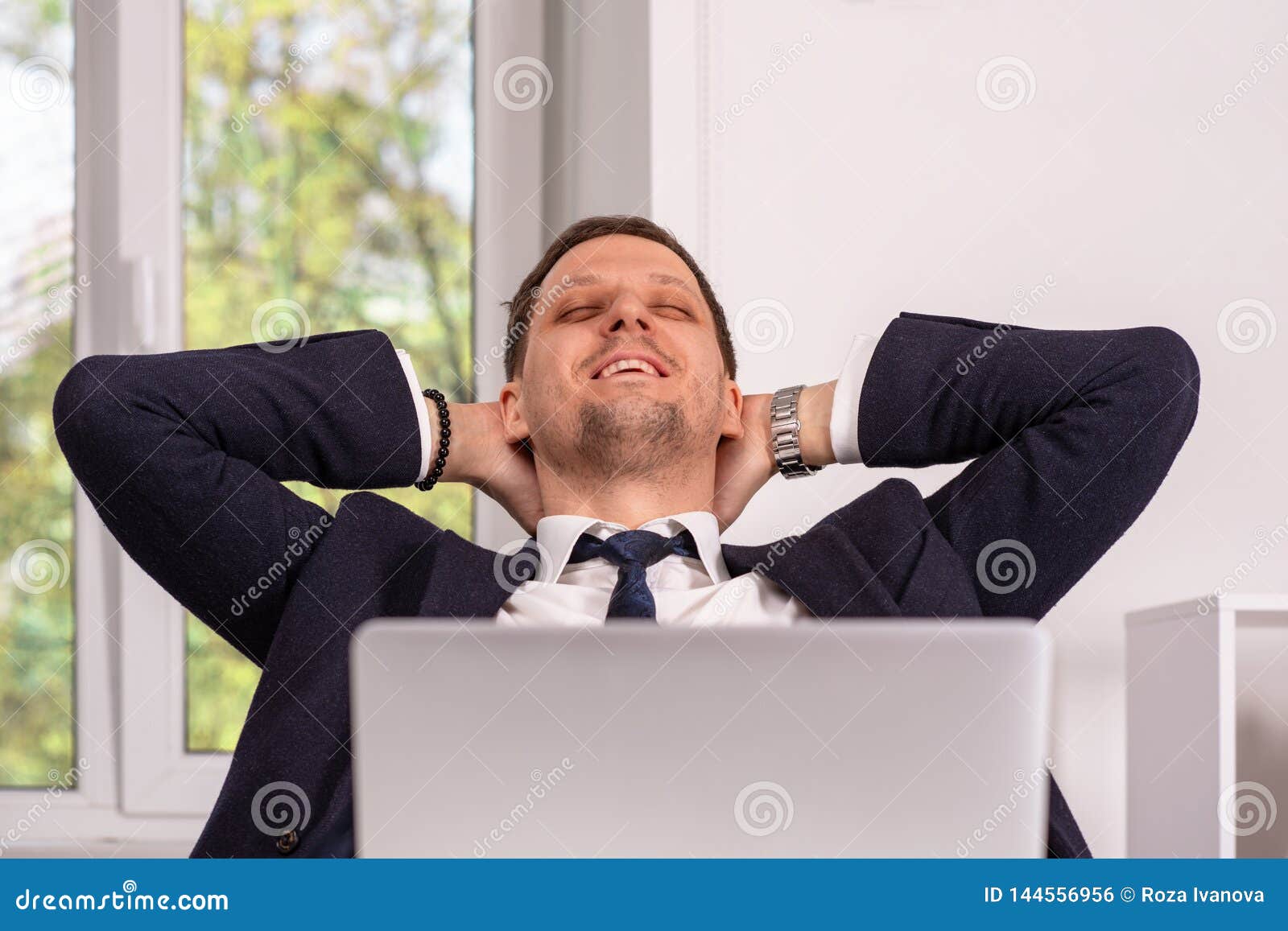 Studio Shot of a Young Smiling Man Sitting with His Hands Behind His ... Studio Shot of a Young Smiling Man Sitting with His Hands Behind His ...