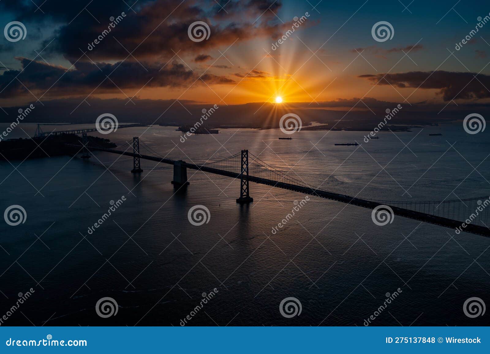 The Sun is Setting Over the Ocean with the Bridge Going into the ...
