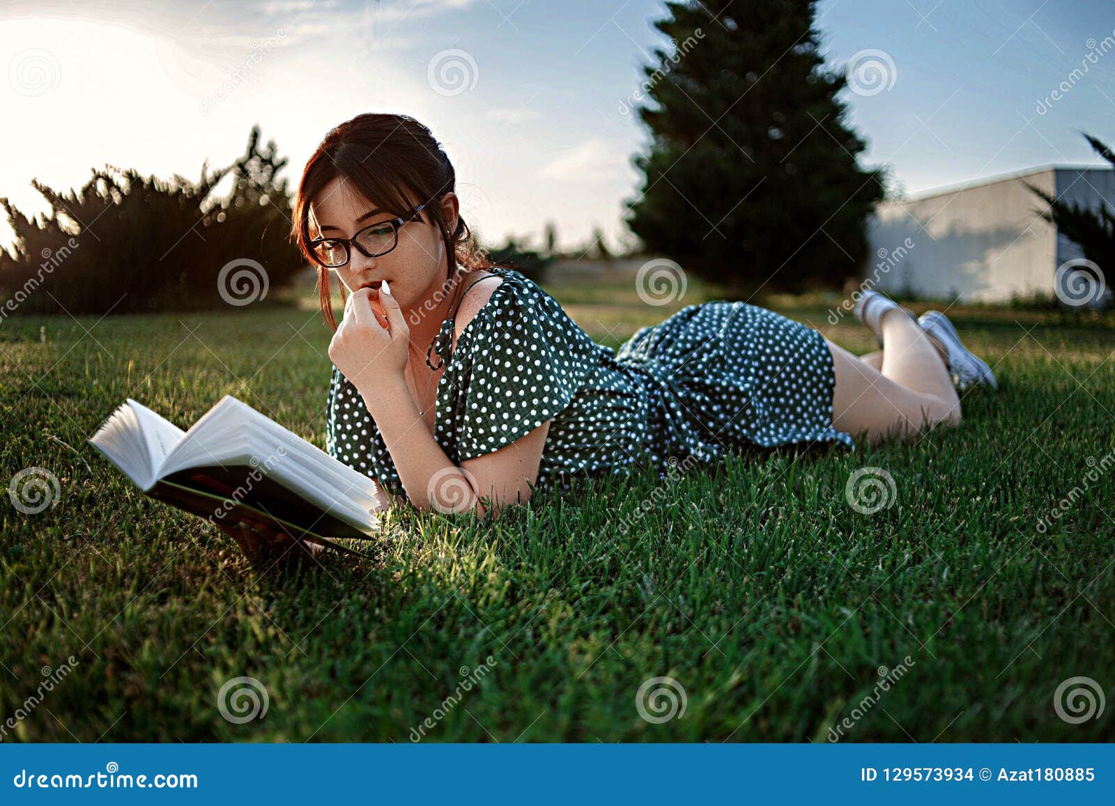Happy Woman Lying On Green Grass Reading A Book In The Park Outdoors