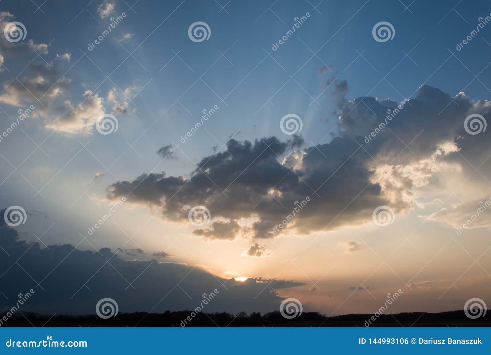 The Sun Setting Behind Clouds and Sunrays Above the Horizon Stock Photo ...