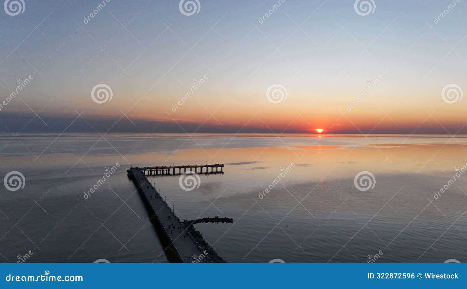 The Sun Setting Behind a Dock Over Water with a Train Bridge Going into ...