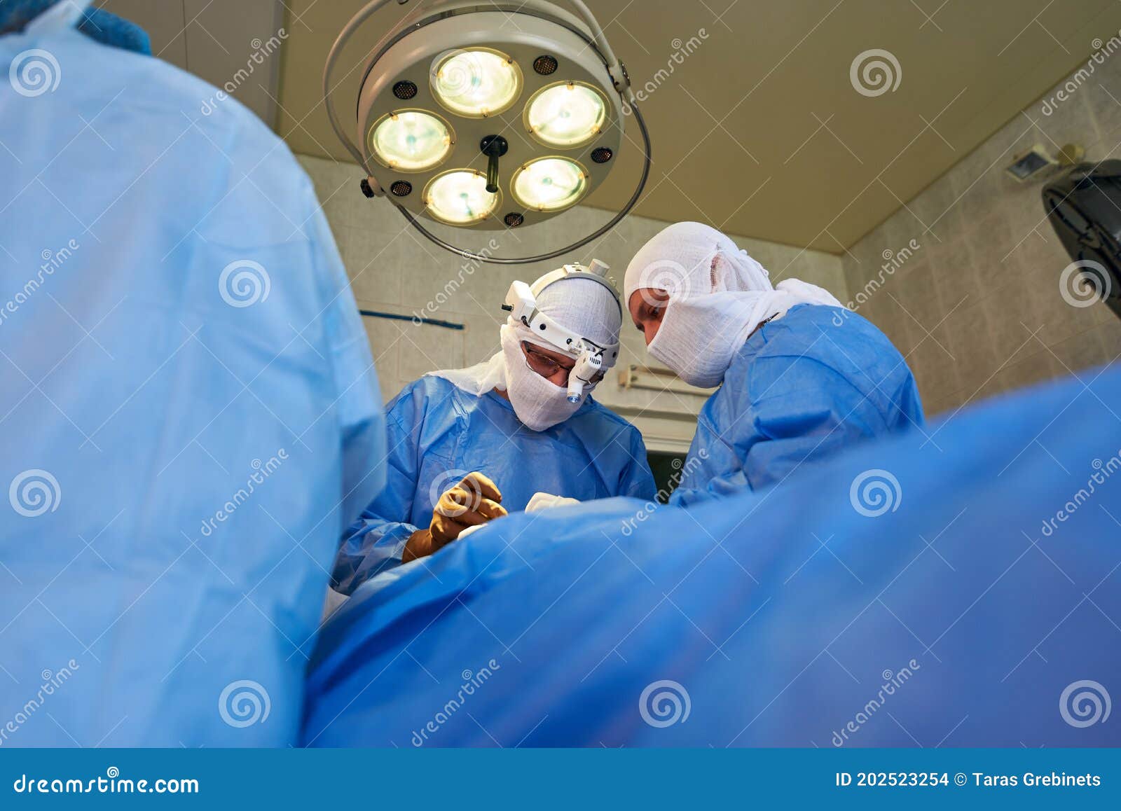 Surgery. Bottom-up View of the Faces of Surgeons Under a Round Surgical ...