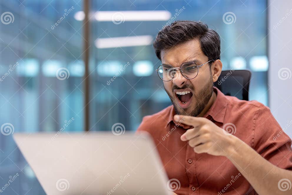 Surprised Man with Glasses Sitting at Desk Pointing at Laptop Screen ...