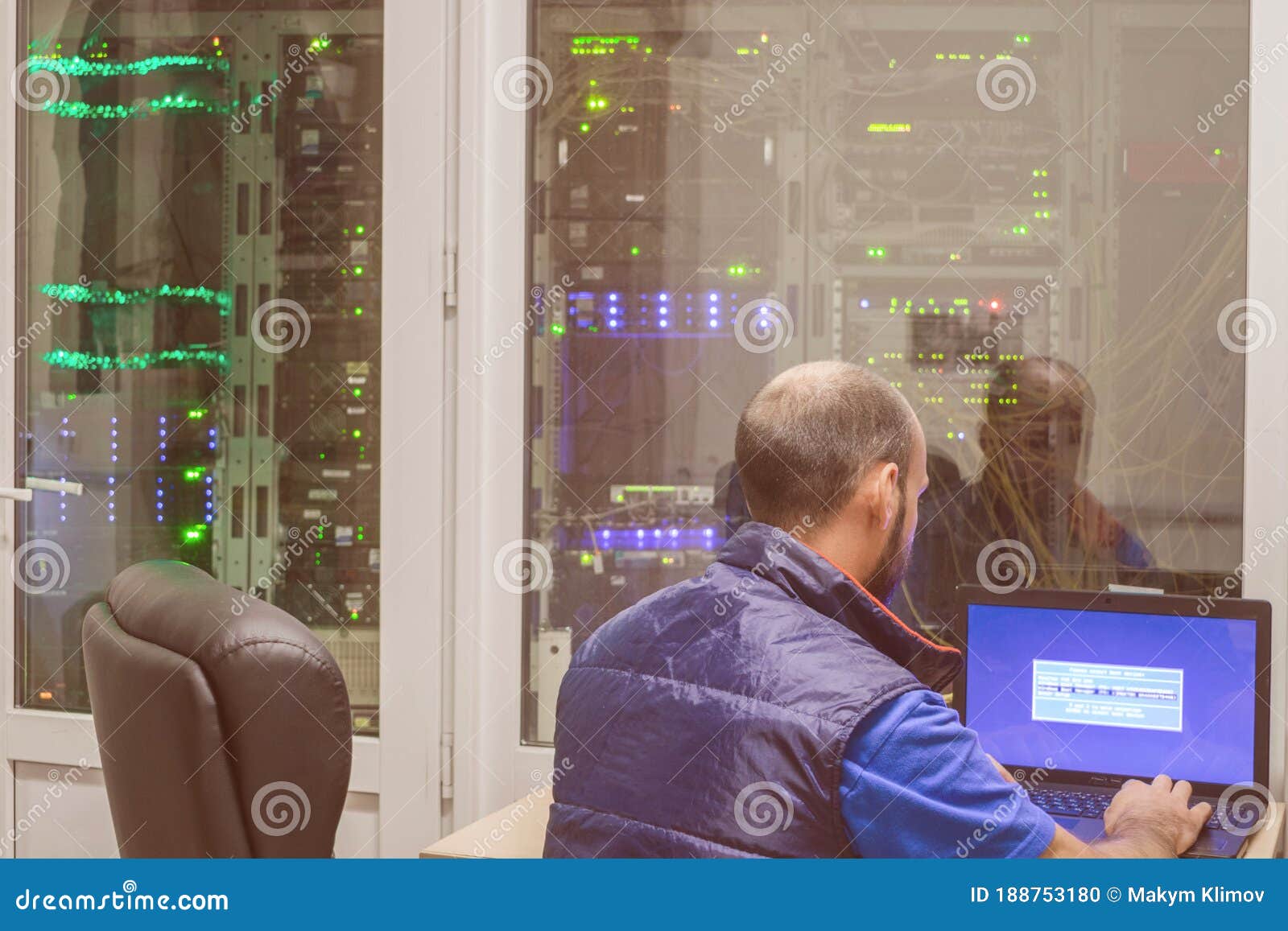 A System Administrator with a Laptop Sits in Front of the Glass Door of ...