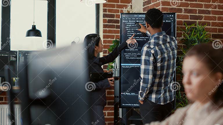 System Developers Analyzing Code On Wall Screen Tv Looking For Errors Comparing Results On