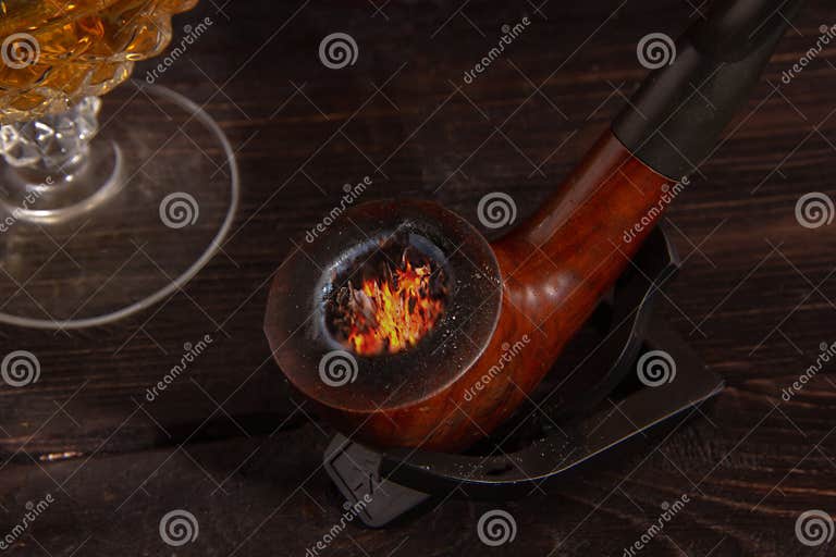 On the Table There is a Glass of Whiskey and a Lighted Smoking Pipe ...