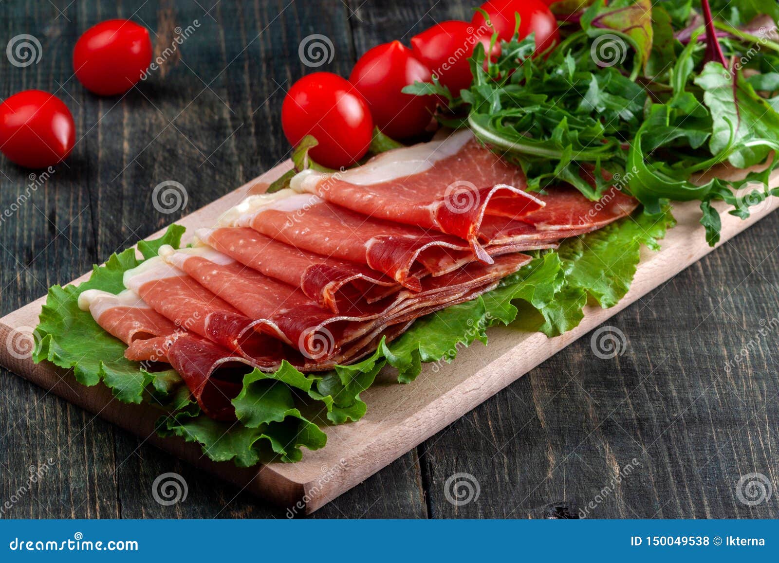 On the Table is a Wooden Cutting Board with Sliced Jamon, Tomatoes and ...