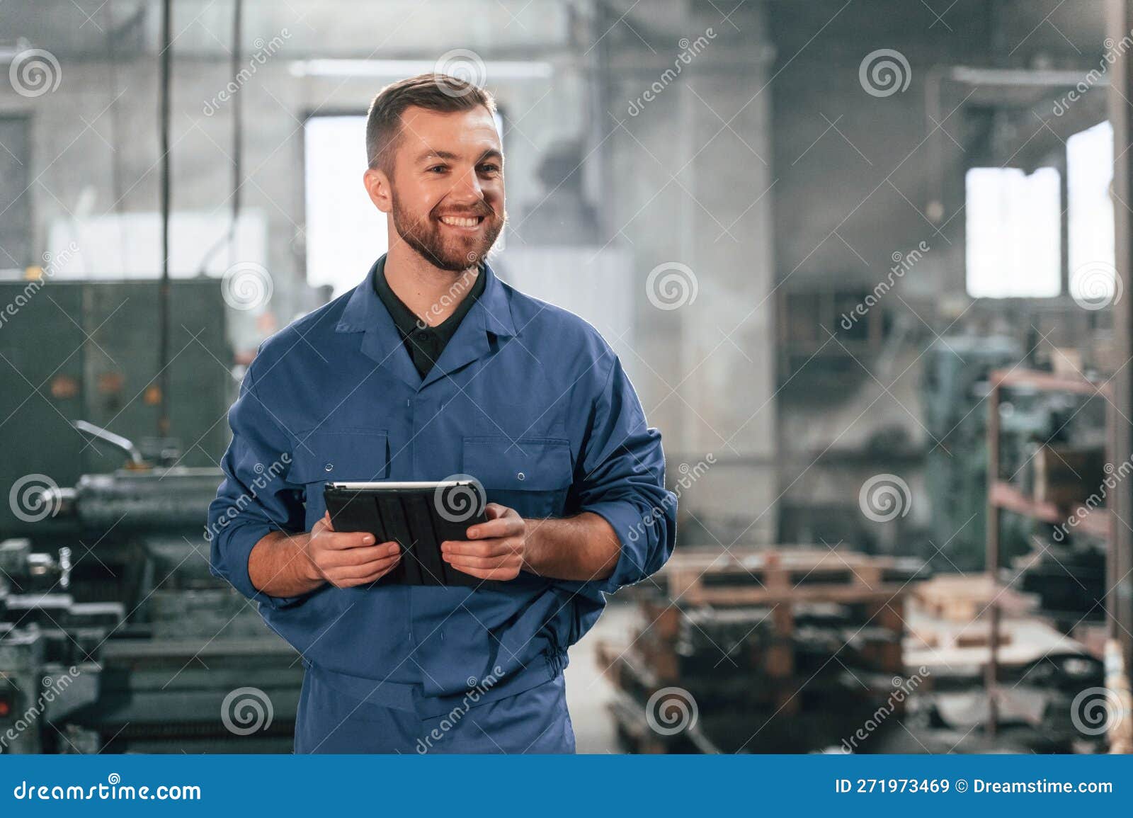 With Tablet in Hands. Factory Worker in Blue Uniform is Indoors Stock ...